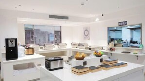 Uma cozinha moderna com bancadas brancas, uma máquina de café e uma grande janela com vista para a cidade.