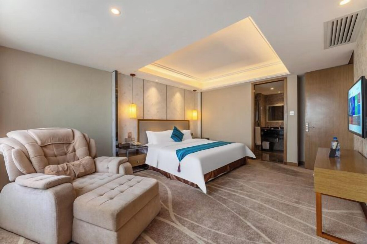 Quarto de hotel com uma cama grande, uma cadeira de massagem, uma escrivaninha e uma televisão.