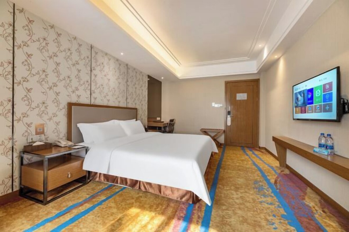 Quarto de hotel com uma cama grande, mesas de cabeceira, uma televisão e piso coberto por carpete.
