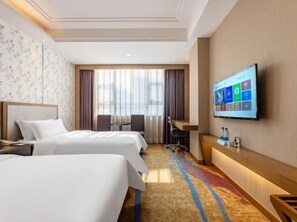 Quarto de hotel com duas camas, uma escrivaninha, televisão e janela com cortinas.