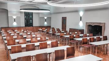 Uma sala de conferências com várias mesas e cadeiras, teto estampado e lareira.