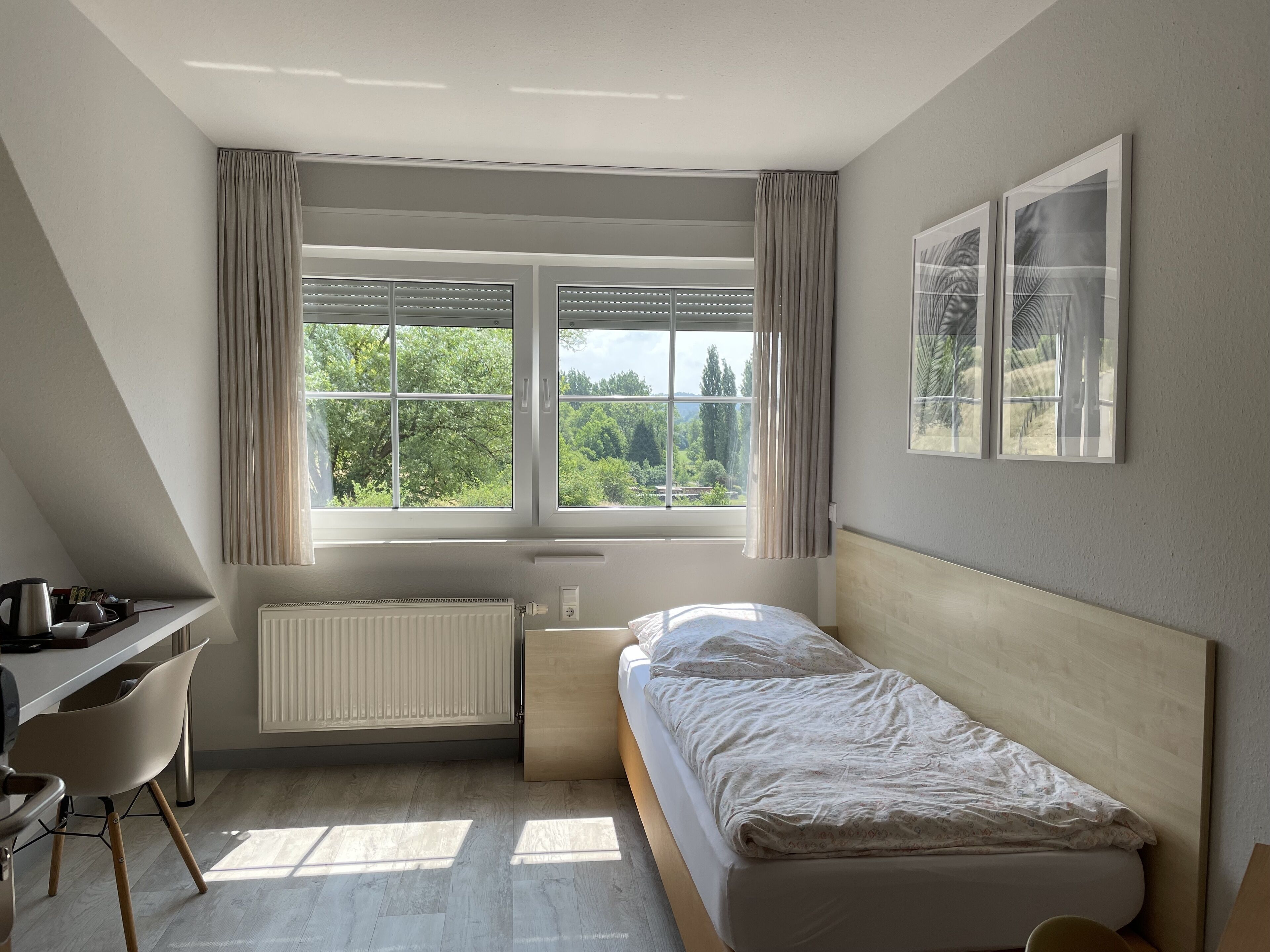 Quarto com cama, escrivaninha, cadeira, radiador e janela com cortinas.
