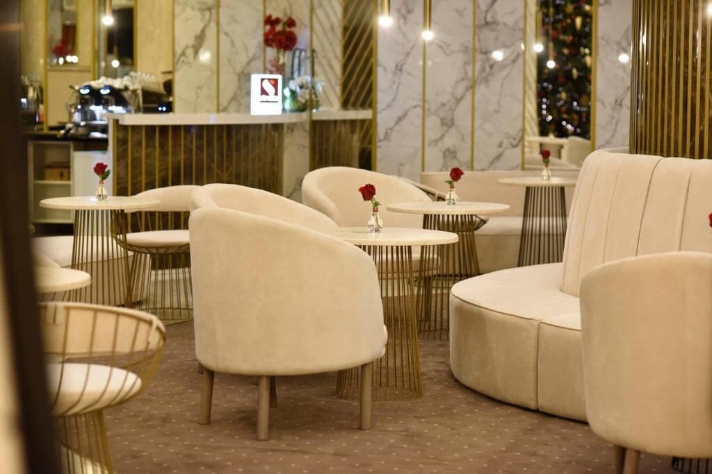 Uma área de lounge moderna com assentos confortáveis e mesas redondas, com uma parede de mármore e uma árvore de Natal ao fundo.