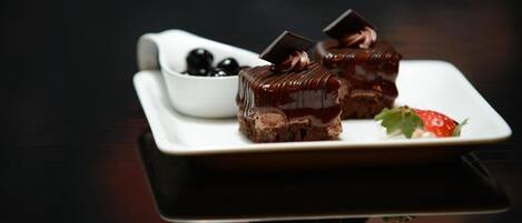 Um prato de sobremesa com bolo de chocolate e morango sobre uma superfície espelhada.