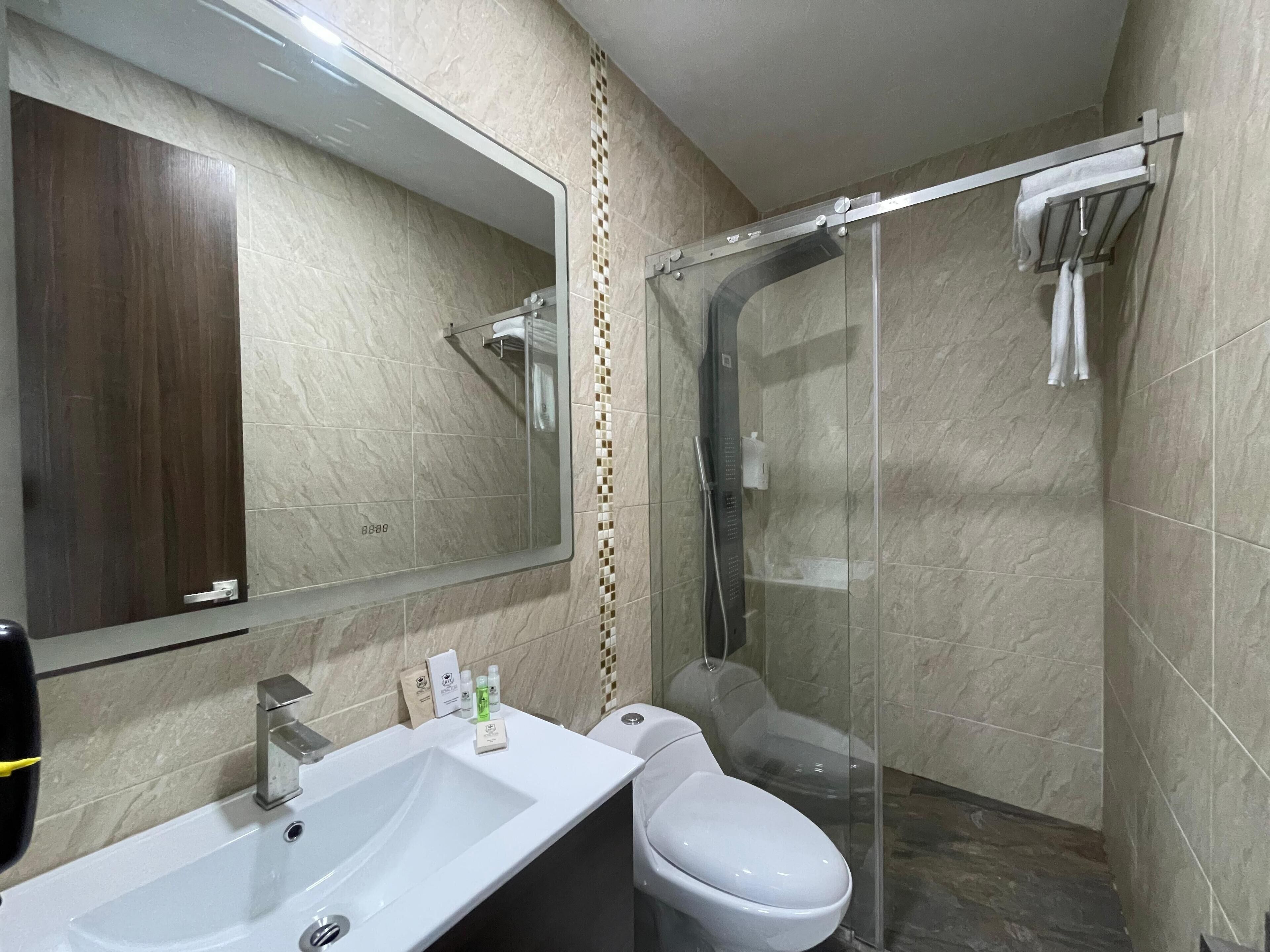 Uma casa de banho moderna com um espelho grande, uma sanita branca, uma casa de wc e uma área de duche com vedação em vidro.