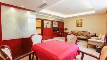 Quarto de hotel com colcha vermelha, sofá, televisão e um quadro na parede.