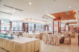 Uma sala de banquetes com mesas redondas e cadeiras, grandes janelas e teto alto.