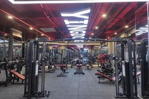 Uma academia com diversos equipamentos de exercícios, espelhos e um letreiro 'YINGDONG' bem visível no teto.