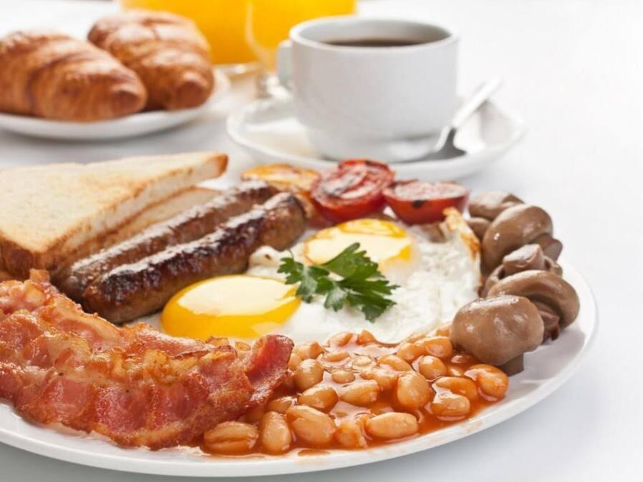 Prato de café da manhã com torradas, salsichas, bacon, ovos, tomates, cogumelos e feijão.