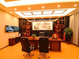 Uma sala de conferências com uma mesa grande, duas cadeiras de escritório, uma televisão fixada na parede e um quadro emoldurado de grandes dimensões.