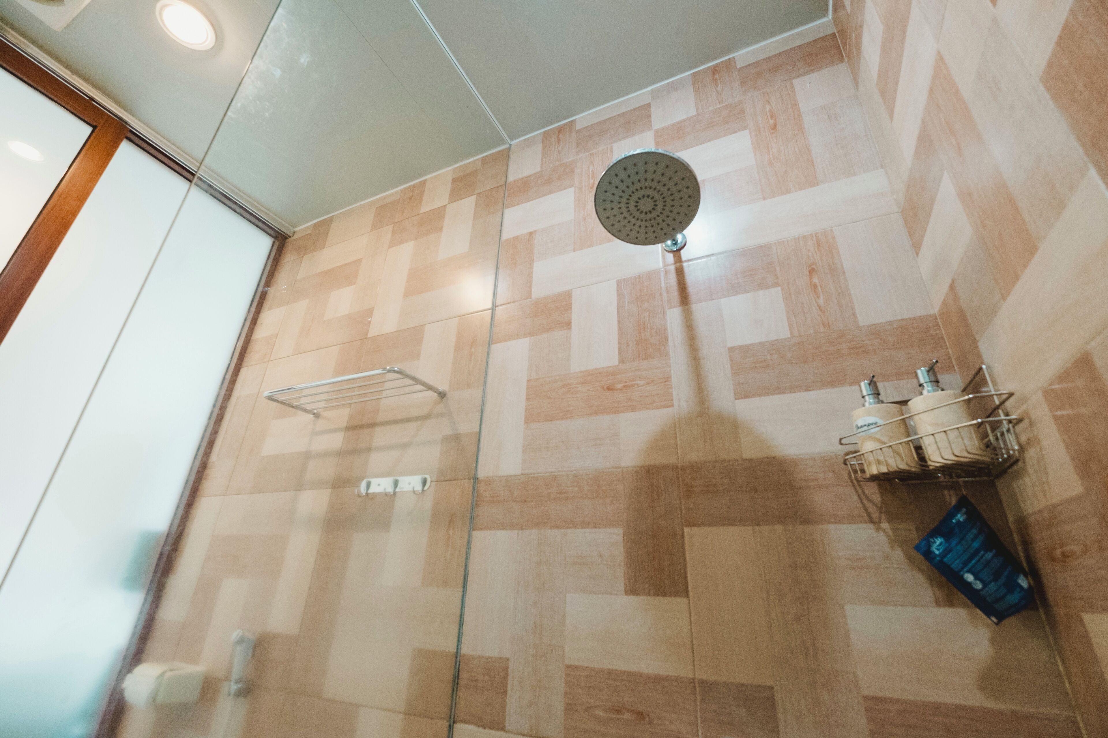 Um chuveiro com porta de vidro, uma luminária no teto e um nicho na parede com produtos de higiene pessoal.