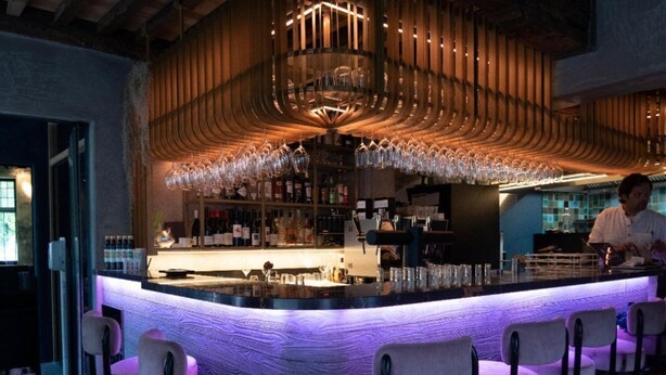 Uma área de bar com balcão curvo, banquetas e um bartender.