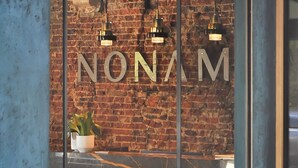 Um interior moderno com parede de tijolos, porta de vidro com a inscrição "NONAM" e luminárias pendentes.