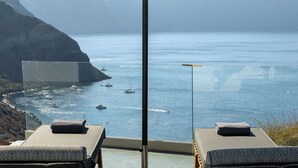 Varanda com vista desobstruída para o mar e barcos, com duas cadeiras de descanso e parapeito de vidro.