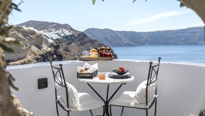 Uma mesa com um buffet de café da manhã, duas cadeiras acolchoadas brancas e uma vista panorâmica da costa montanhosa.