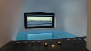 Um quarto de spa com banheira, janela com vista para uma paisagem distante e velas no chão.