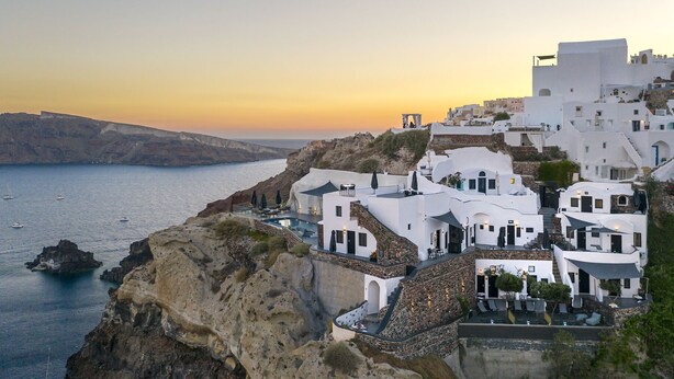 Uma vila costeira com edifícios brancos, um penhasco e vista para o mar.