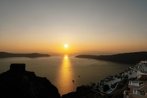 Vista de um pôr do sol costeiro com céu claro, mar calmo e um edifício branco com varandas voltadas para a água.