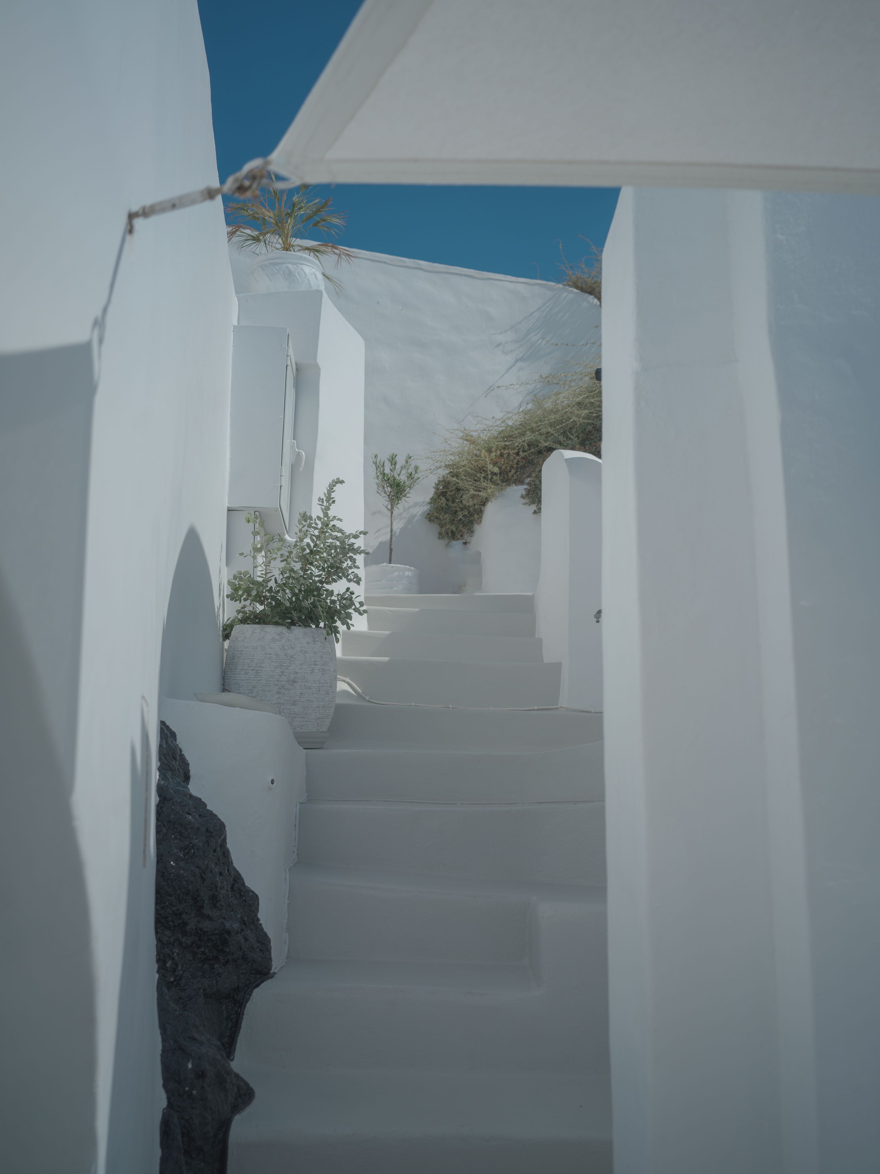 Escadaria branca que leva a um espaço coberto com plantas em vasos e um céu azul claro.