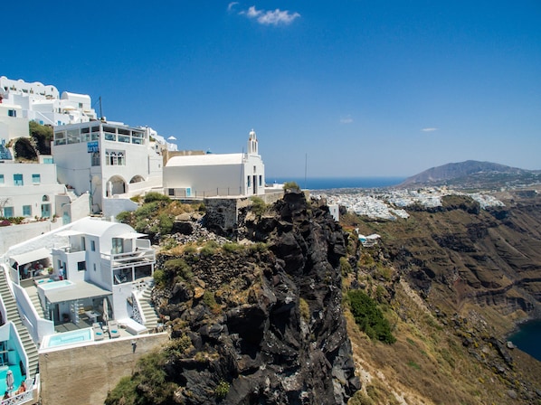 Uma vila costeira com edifícios brancos, um penhasco rochoso e vista para o mar.