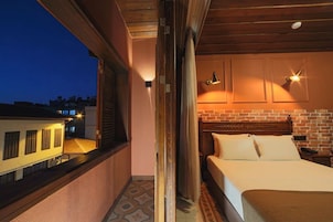 Quarto com parede de tijolos, teto de madeira e uma grande janela com vista para a cidade à noite.