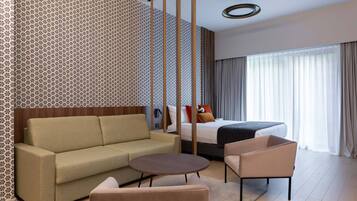 Quarto de hotel com sofá, poltrona, mesa redonda e cama com dossel.