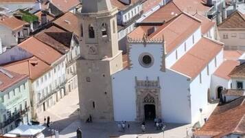 Uma praça histórica na cidade, com uma igreja imponente e um campanário, rodeada por edifícios tradicionais com telhados de terracota.