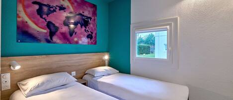 Quarto de hotel com duas camas, uma pintura abstrata grande, uma janela com vista para vegetação e um ponto de luz na parede.
