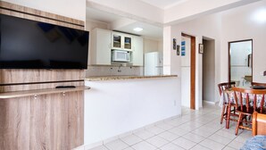 Cozinha moderna com televisão de tela plana, micro-ondas e geladeira. Há uma área de jantar com mesa e cadeiras.