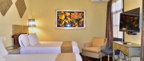 Quarto de hotel com duas camas, uma escrivaninha, uma cadeira, uma televisão e um quadro na parede.