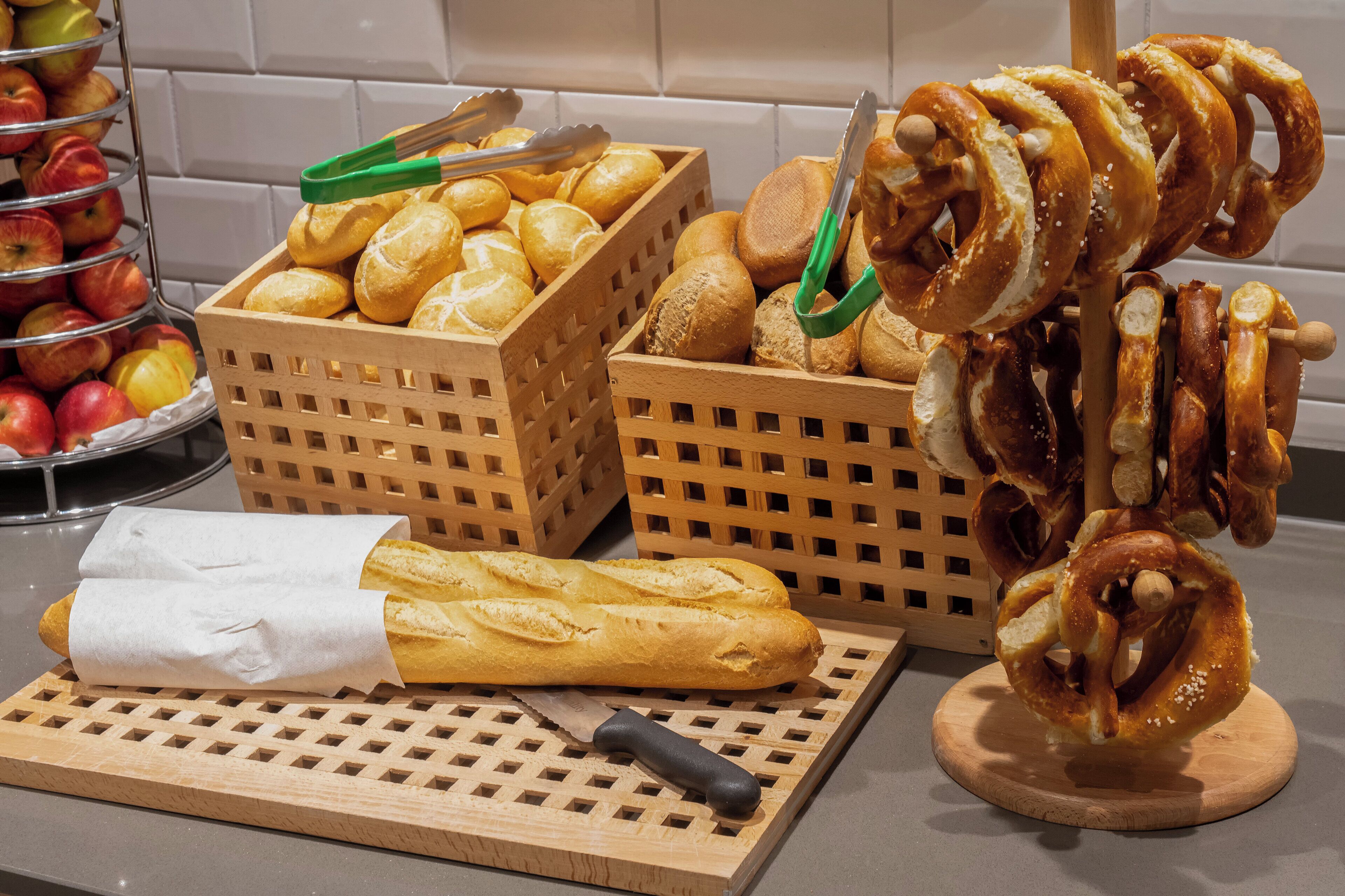 Tábua de madeira com uma baguete, uma faca e um suporte para pretzels.