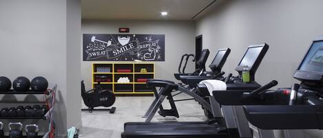 Uma academia com esteiras, aparelhos de musculação e uma parede com frases motivacionais.