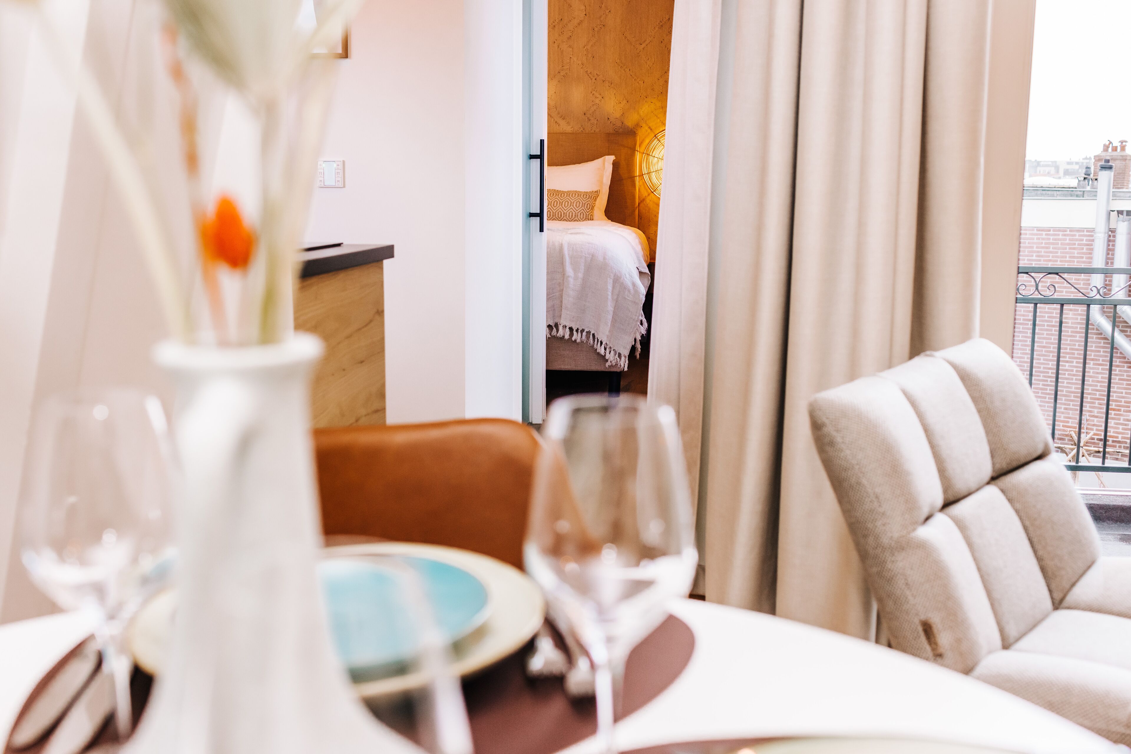 Quarto de hotel com varanda, área de jantar com mesa posta para dois e cama com almofada estampada.