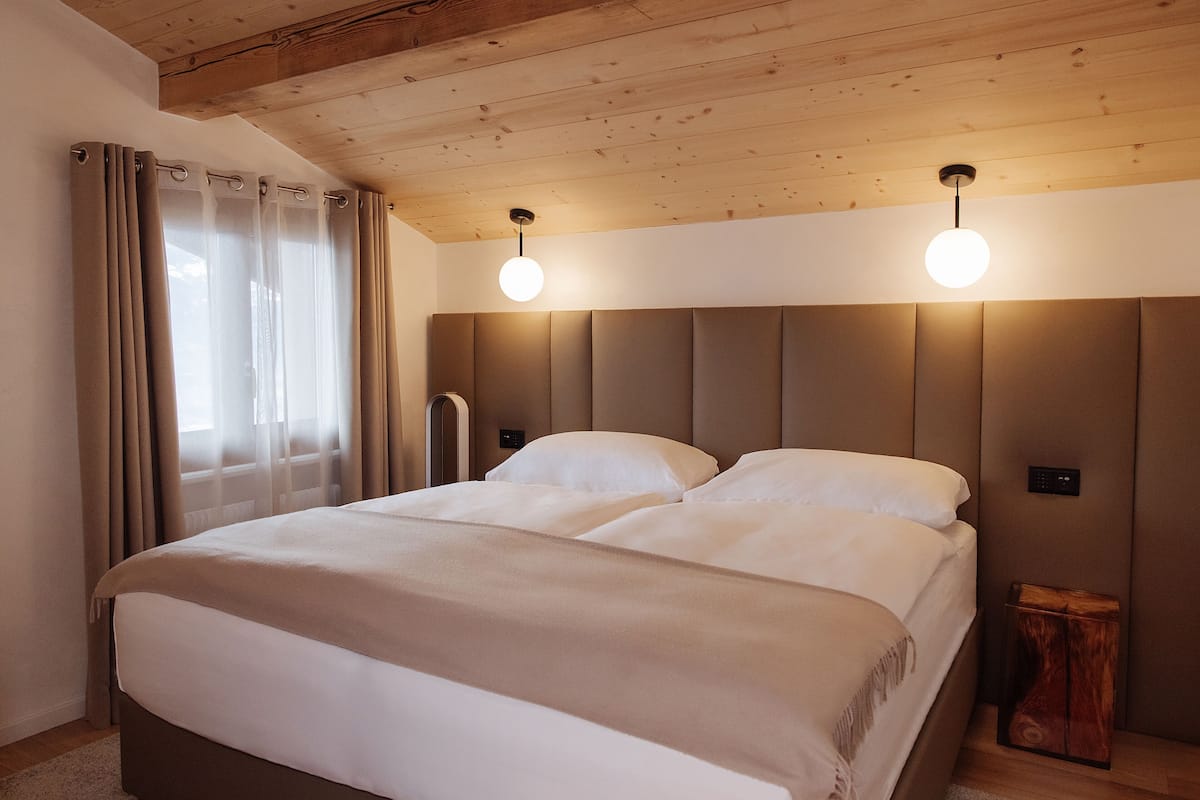 Uma cama de casal com cabeceira, mesa de cabeceira e criadeira.