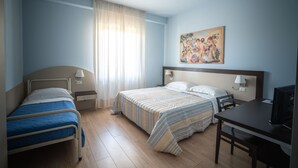 Quarto de hotel com duas camas de solteiro, uma cama de casal, uma mesa e uma televisão.