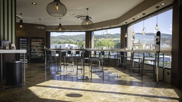 Uma área de bar moderna com pé direito alto, iluminação pendente e vista para uma paisagem montanhosa.