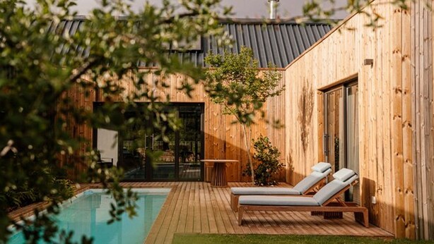 Uma casa moderna de madeira com piscina, espreguiçadeiras e um pequeno jardim.