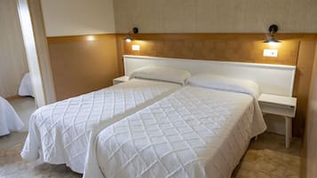 Uma cama de casal com um edredom branco acolchoado, duas mesas de cabeceira com abajures e uma cabeceira de madeira.
