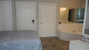 Quarto com cama, penteadeira, banheiro com banheira e duas portas.