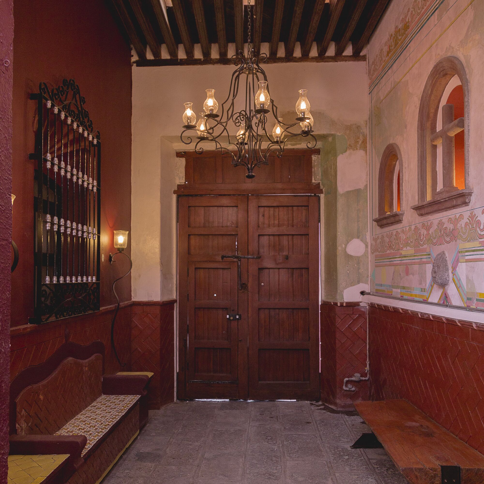 Uma porta de madeira com portão de metal, um banco, um candelabro e uma parede com padrão decorativo.