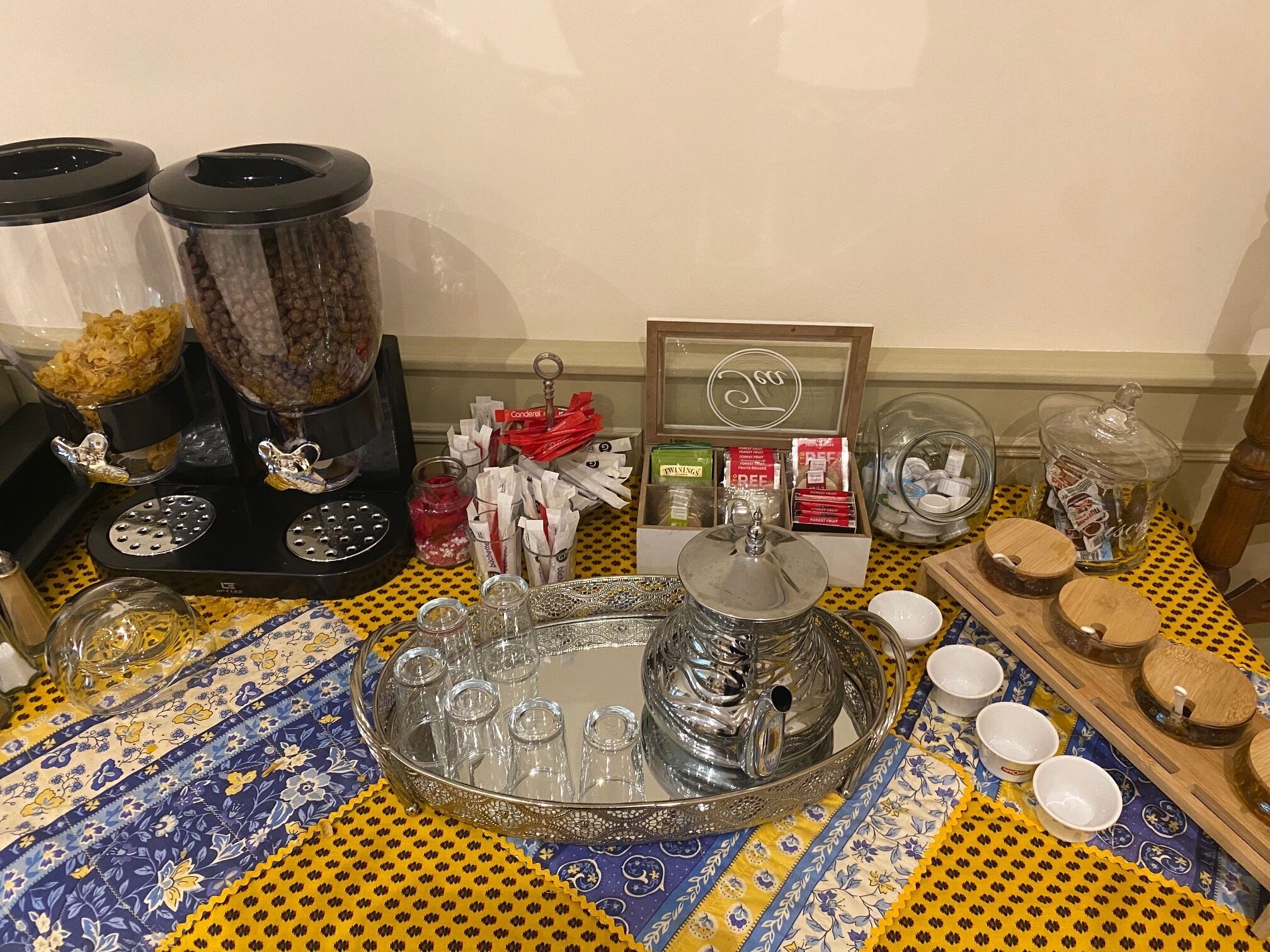 Disposição de buffet de café da manhã com diversos alimentos, máquinas de café e uma bandeja de copos.