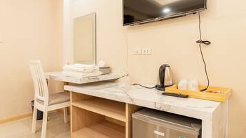 Quarto de hotel com bancada de mármore, televisão montada na parede, pequena cozinha compacta com geladeira e uma cadeira de madeira.