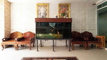Um quarto com um aquário, dois sofás de madeira, um tapete estampado e dois retratos emoldurados na parede.