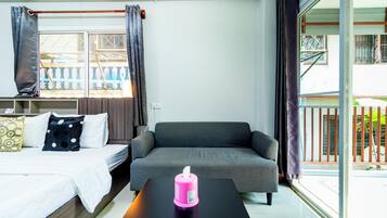 Quarto de hotel moderno com uma cama, um sofá cinzento, uma mesa preta e um objeto rosa sobre a mesa.
