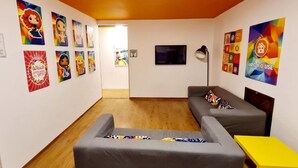 Uma sala de estar com sofás cinzas, uma mesa amarela e obras de arte coloridas nas paredes.