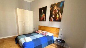 Quarto com cama, guarda-roupa e duas pinturas penduradas na parede.