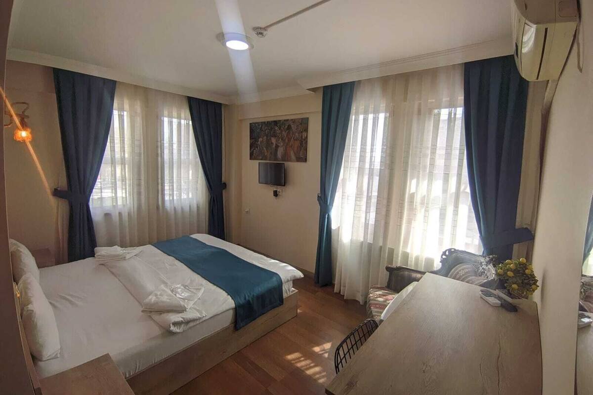 Quarto de hotel com cama, escrivaninha, cadeira, televisão e um quadro na parede.