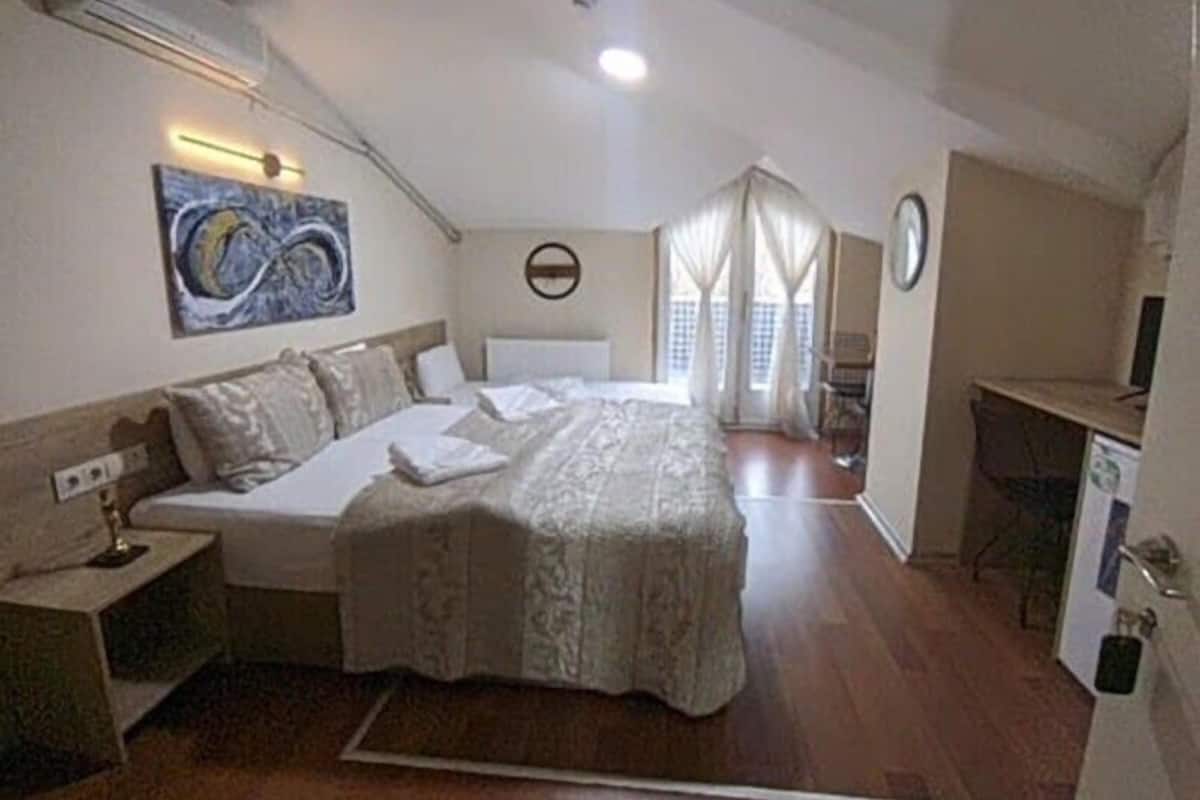 Quarto com cama, mesas de cabeceira, ar condicionado fixado na parede e janela com cortinas.