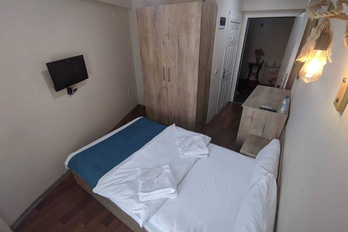 Um quarto com cama, guarda-roupa, escrivaninha e televisão.