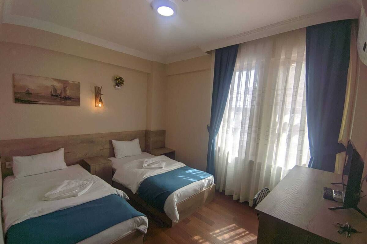 Quarto de hotel com duas camas, uma secretária e um quadro na parede.